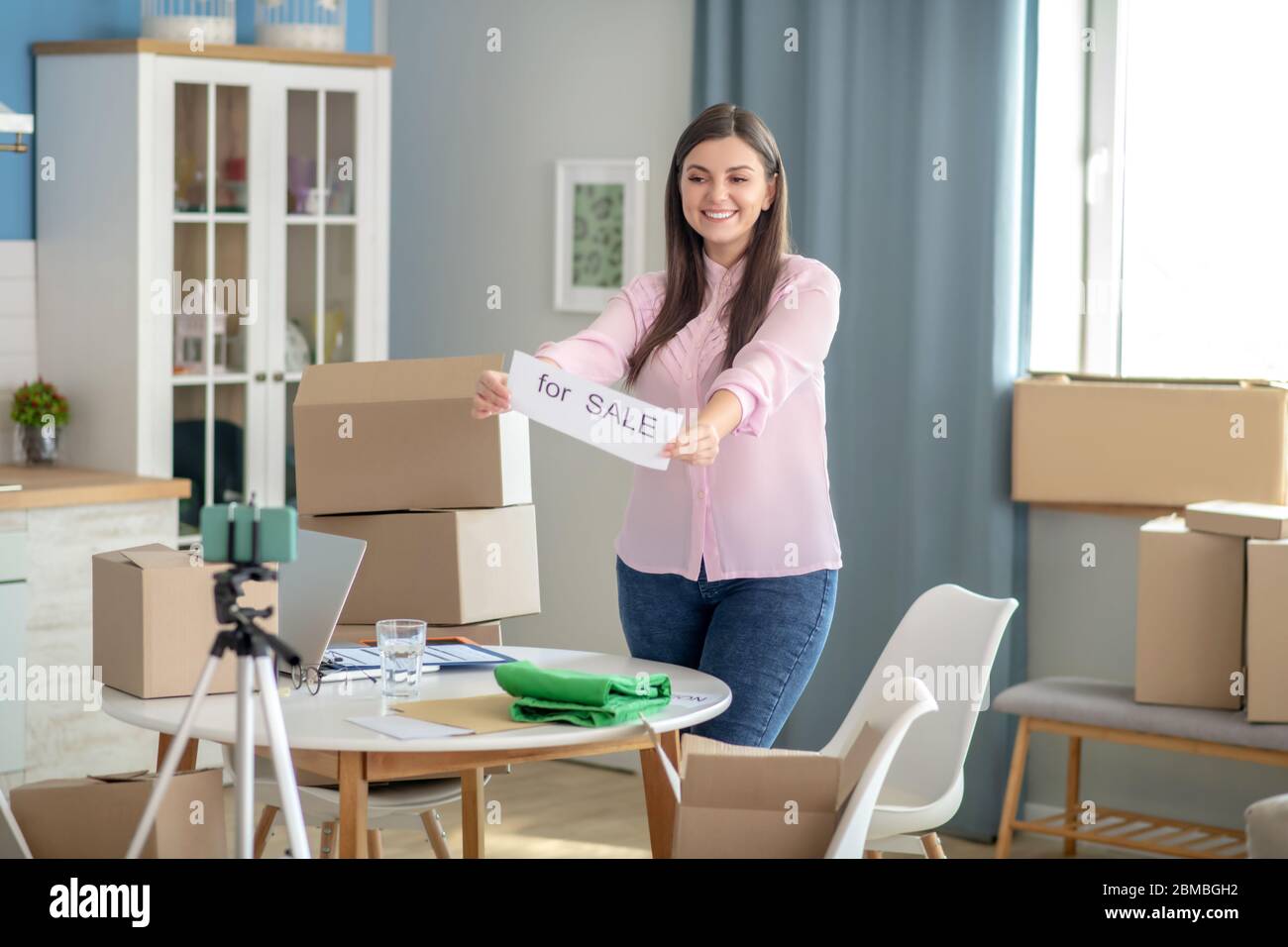 Dark-haired young woman holding a table for sale before the camera ...