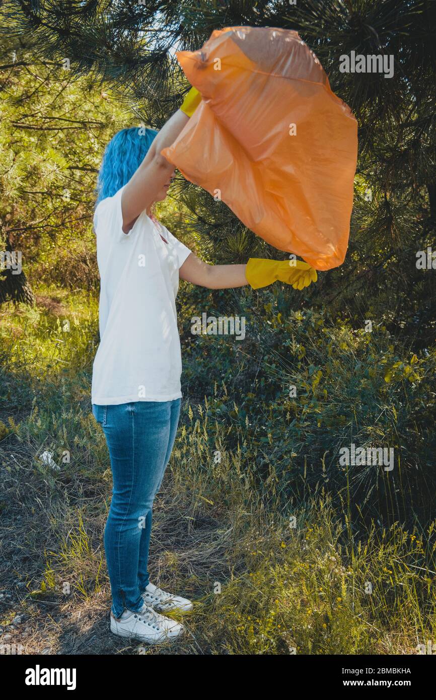 A female emptying the plastic garbage bag in a green environment ...