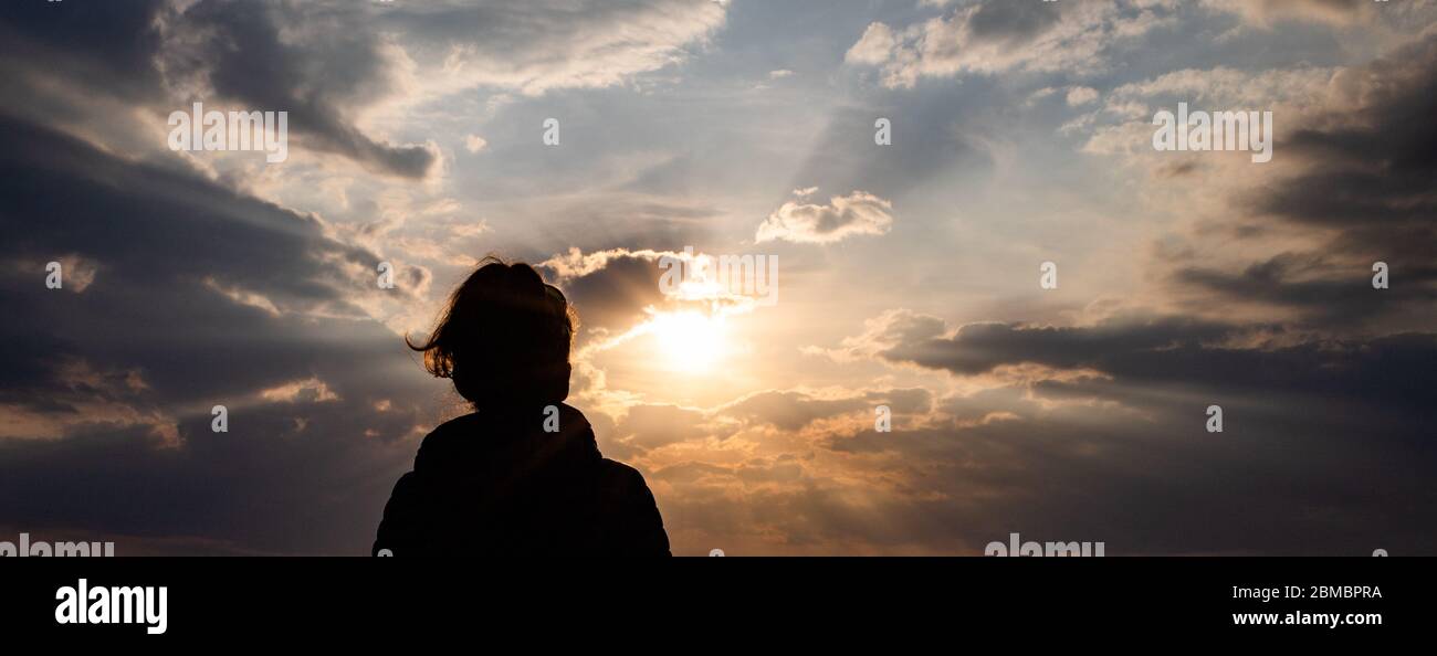 panorama woman head looking at sun breaking through clouds at sunset ...