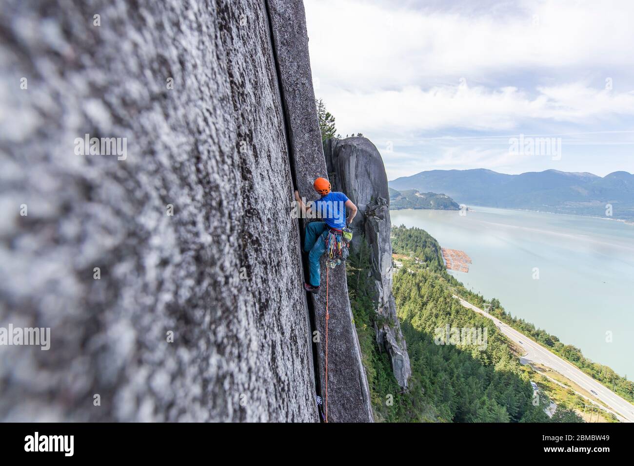 Side view of man climbing multi pitch route on pillar with ocean view ...