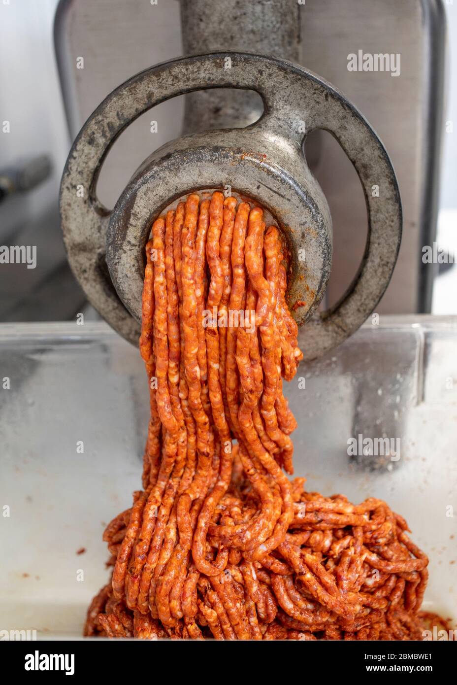 A frontal view of ground meat coming out of the grinder at a butchers ...