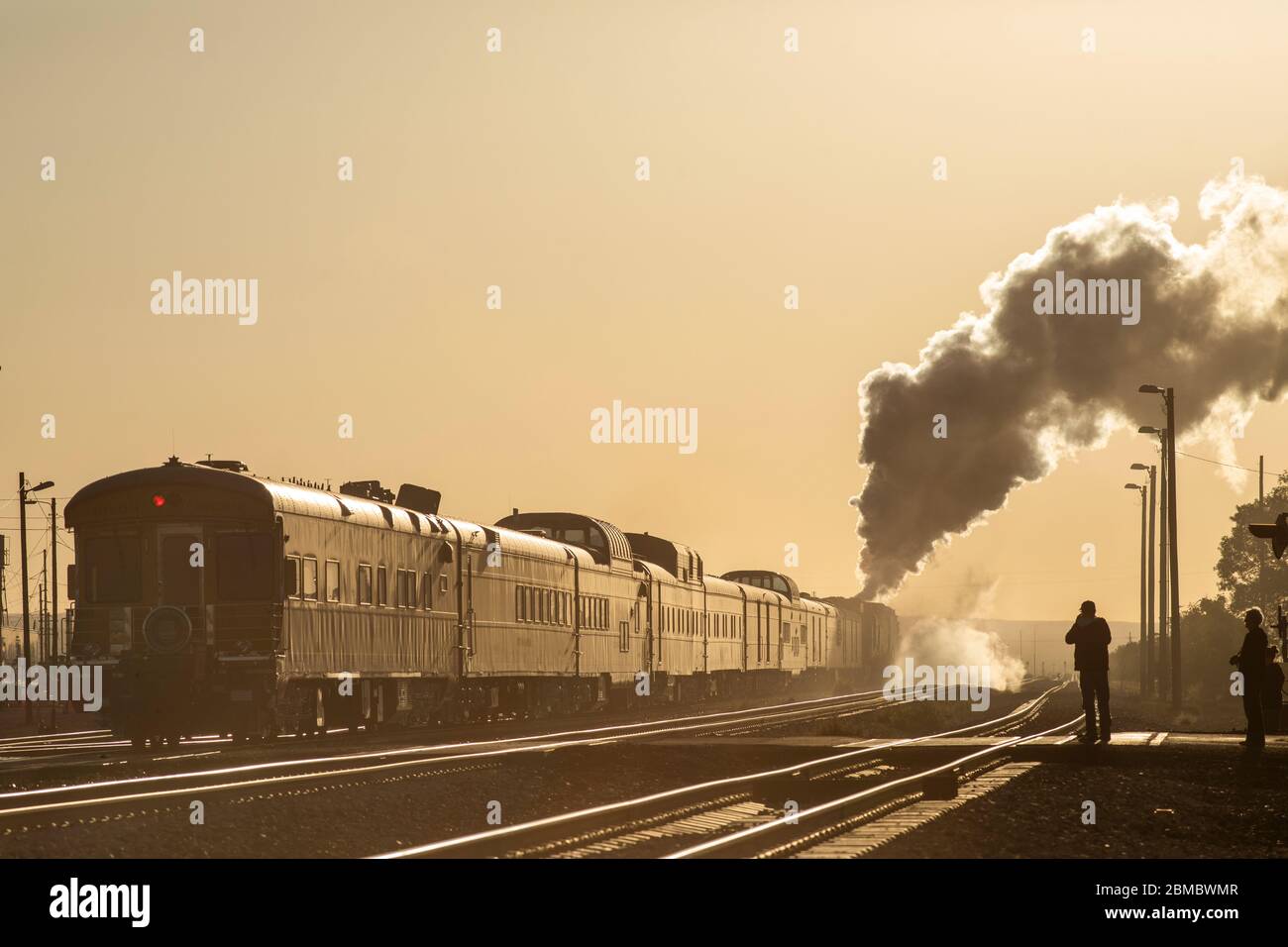 End of a passenger train led by steam engine passes by into yellow sky ...