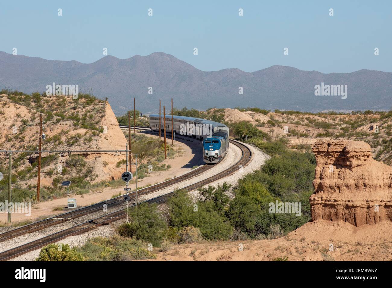 Amtrak passenger train approaches in desert landscape mountains behind ...