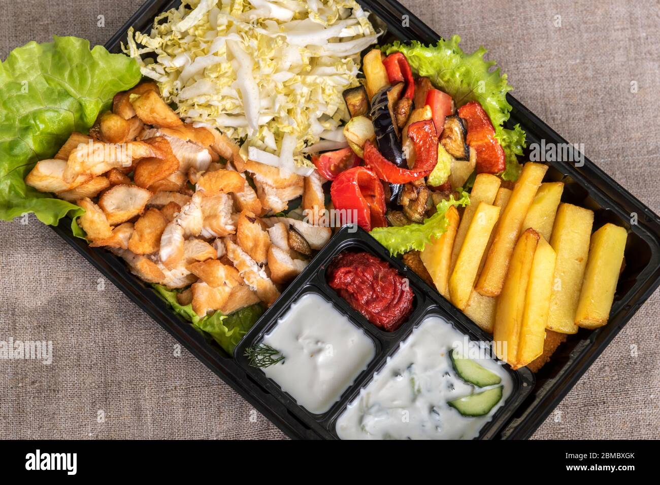 Traditional doner kebab in a black plastic container, sour cream, fried ...