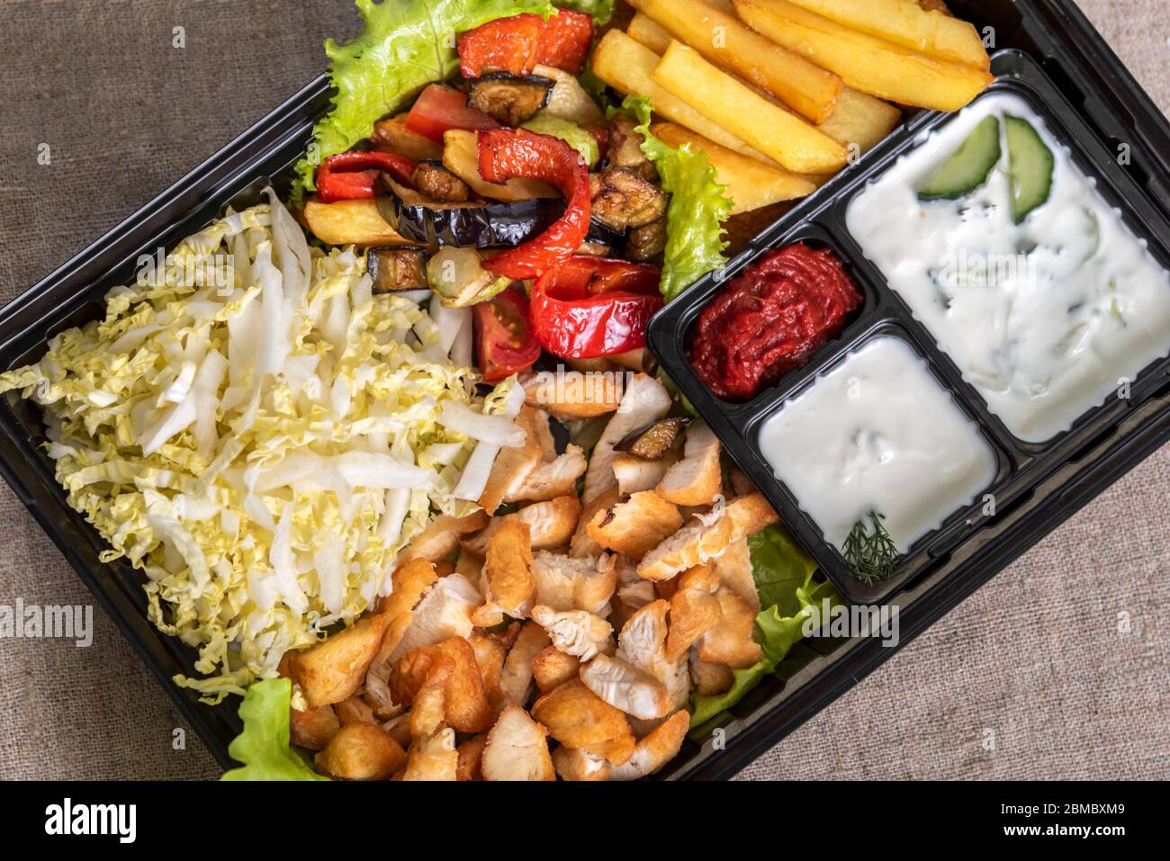 Traditional doner kebab in a black plastic container, sour cream, fried ...