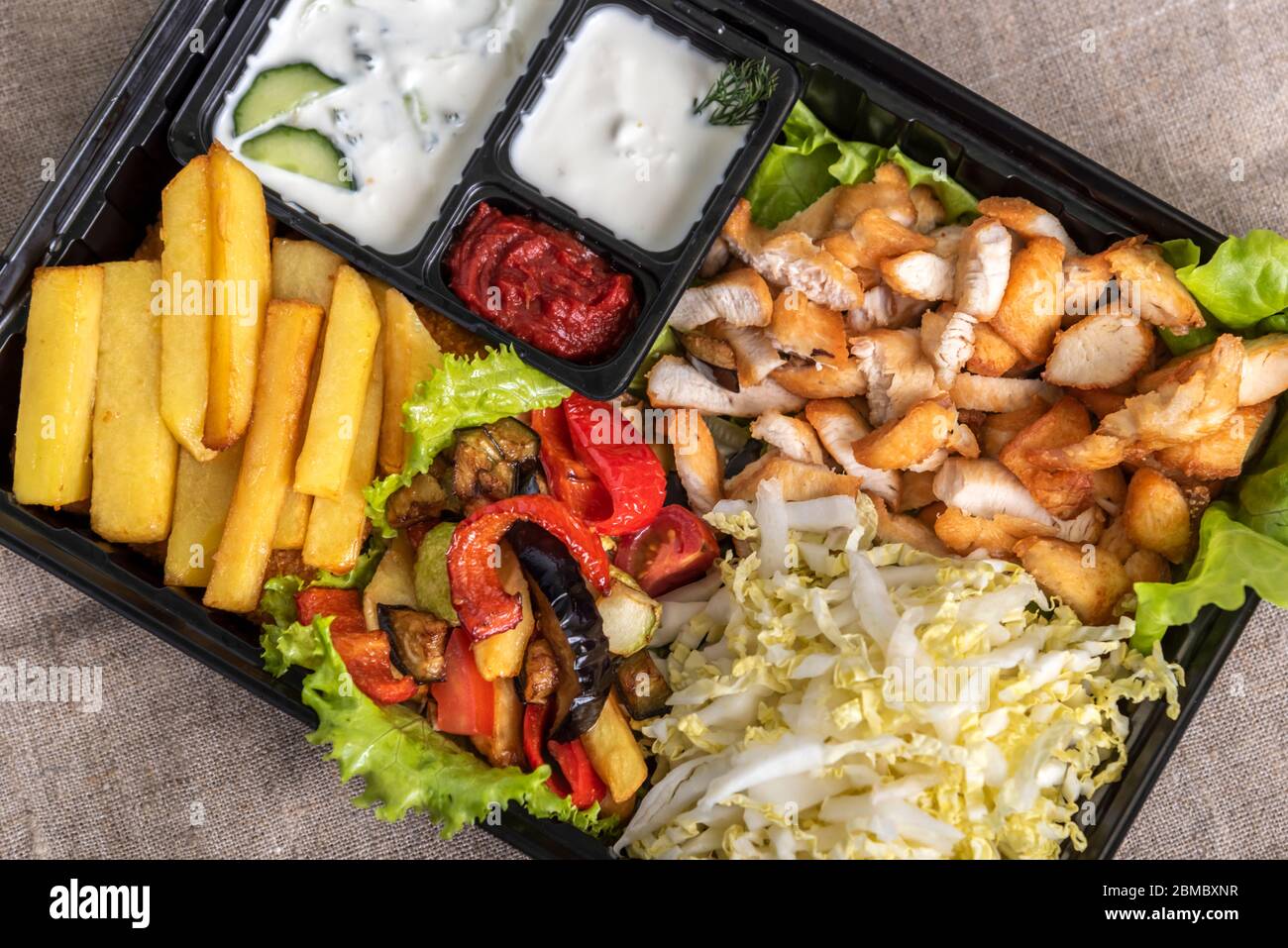 Traditional doner kebab in a black plastic container, sour cream, fried ...