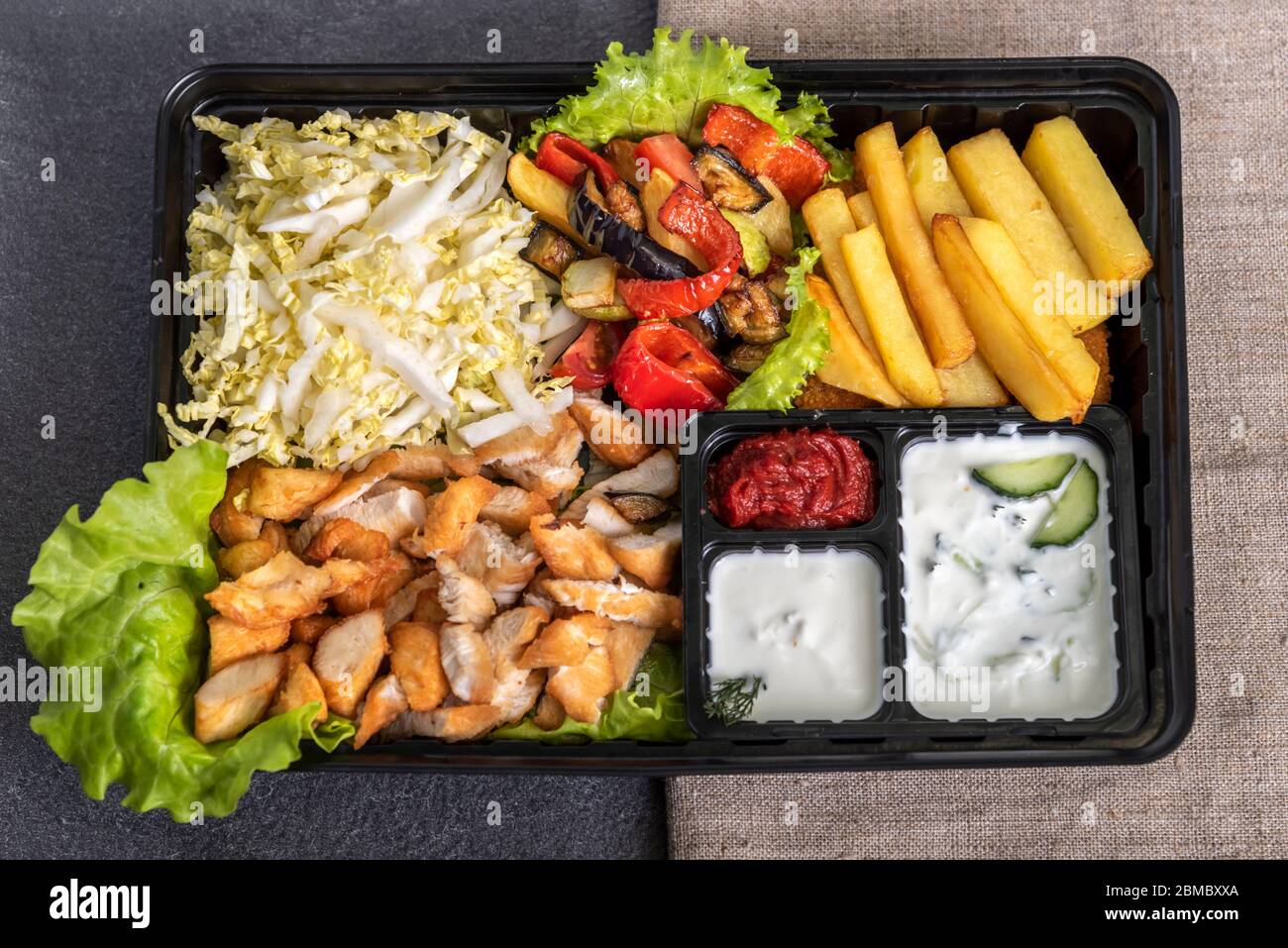 Traditional doner kebab in a black plastic container, sour cream, fried ...