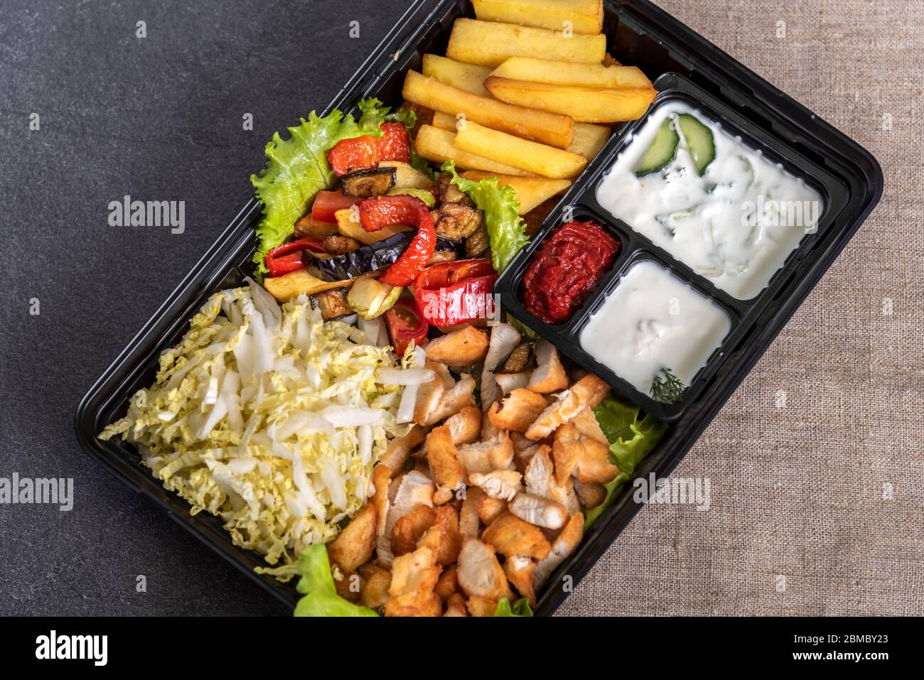 Traditional doner kebab in a black plastic container, sour cream, fried ...