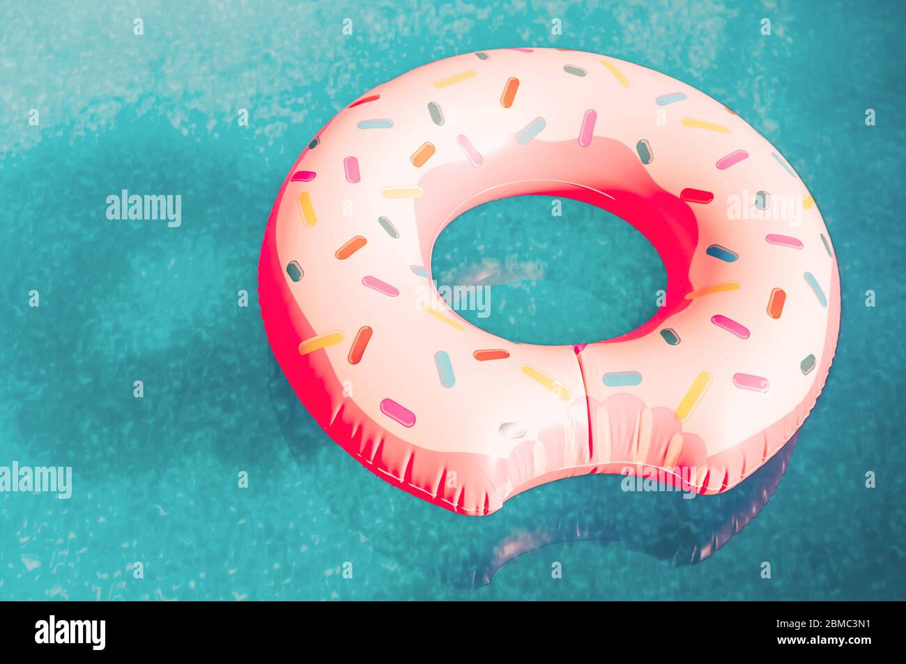 An inflatable pink donut with white icing floats in a blue pool. An ...