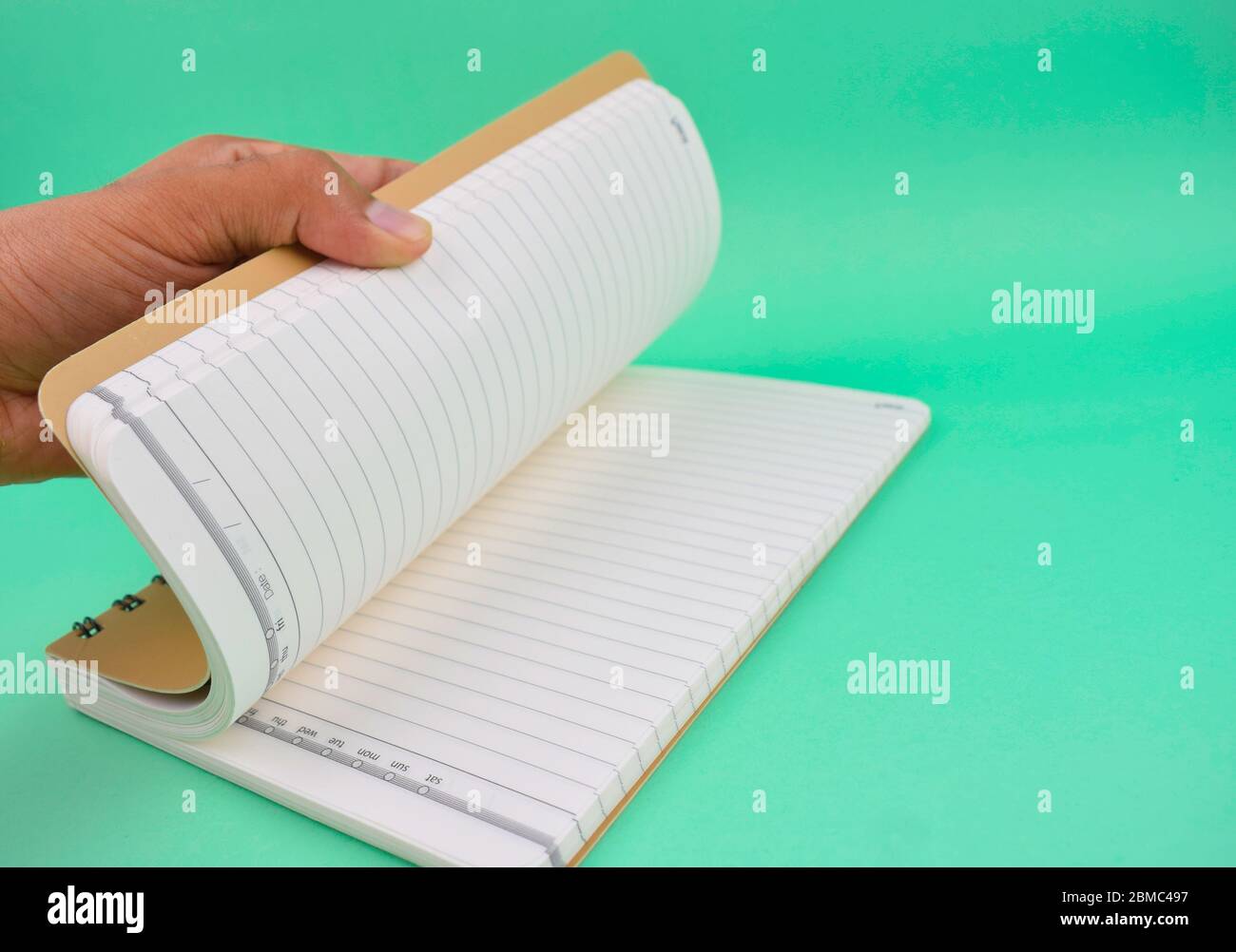 Person opening a white note paper diary placed on an isolated light ...