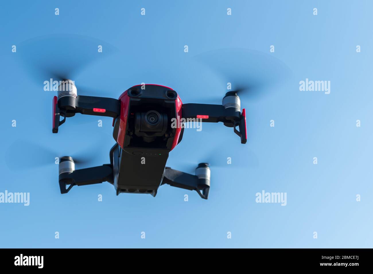 Small sized red drone with high resolution camera hovering in air for ...