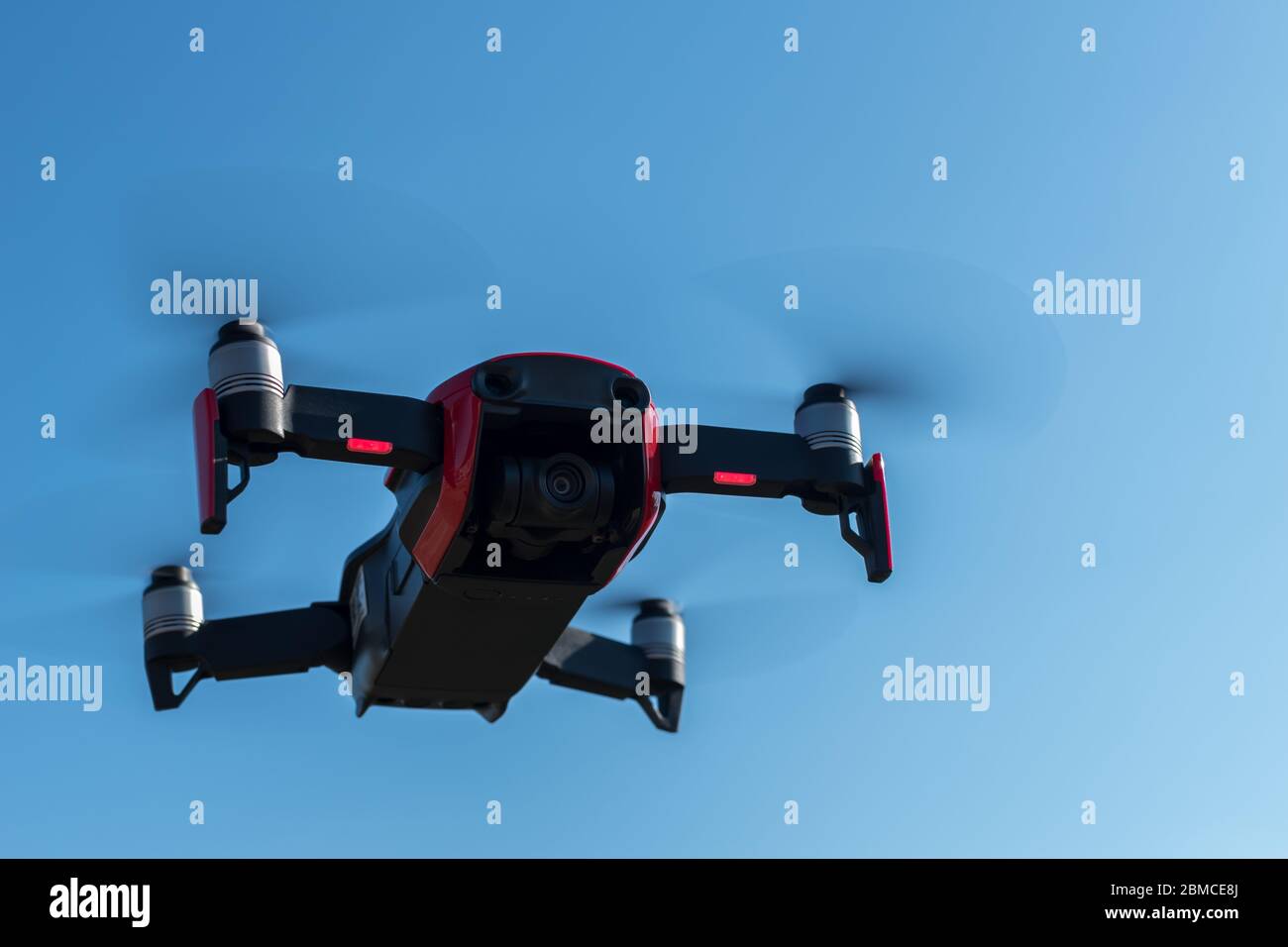 Small sized red drone with high resolution camera hovering in air for ...