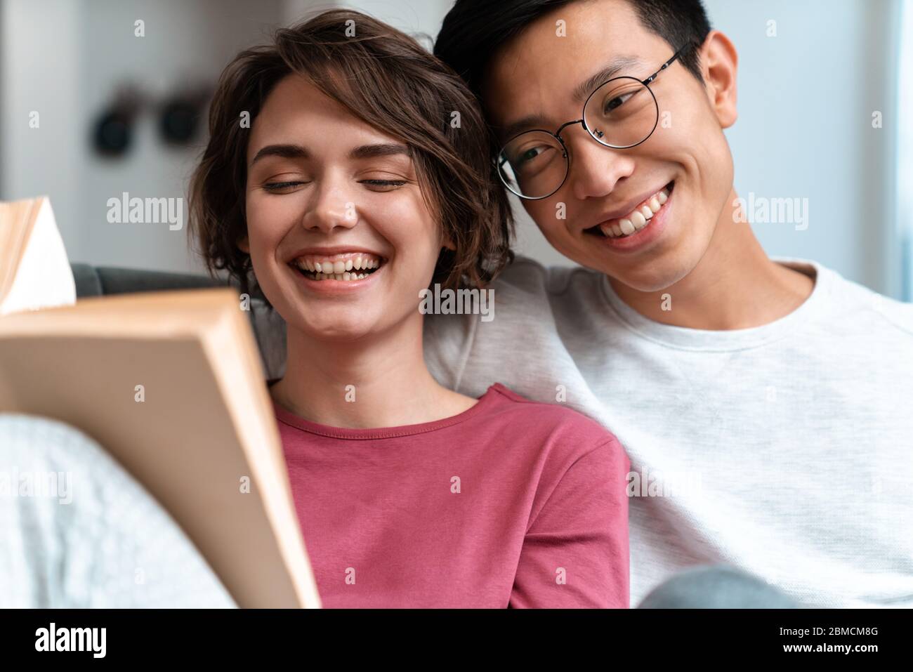 Photo of happy multinational couple reading book and laughing while ...