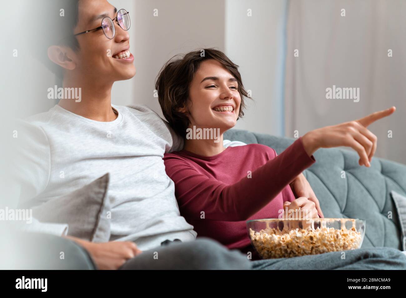 Photo of joyful multinational couple eating popcorn and watching movie ...