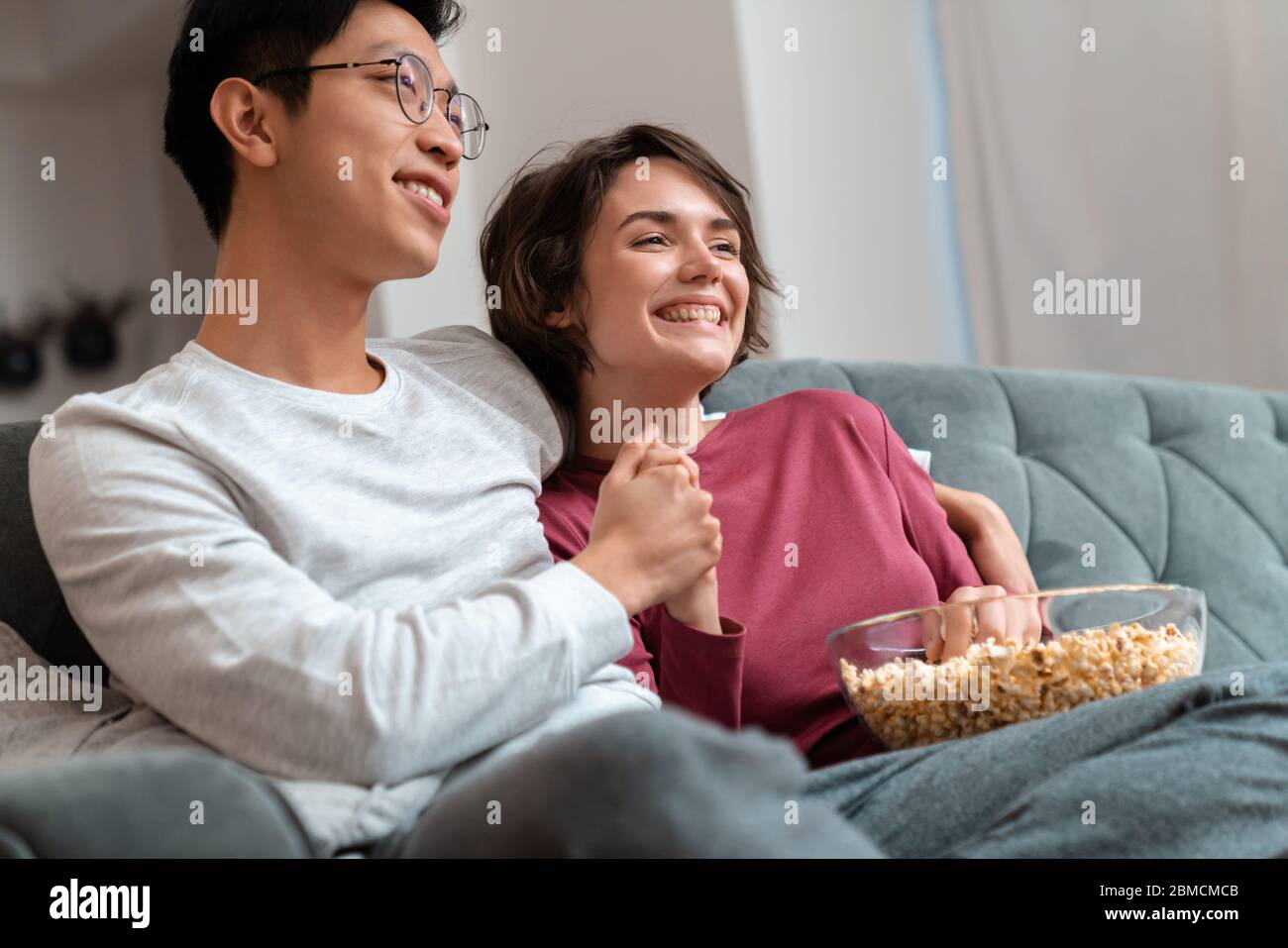 Photo of joyful multinational couple eating popcorn and watching movie ...