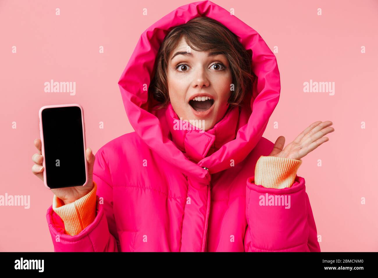 Portrait of nice excited woman in warm coat showing cellphone and ...