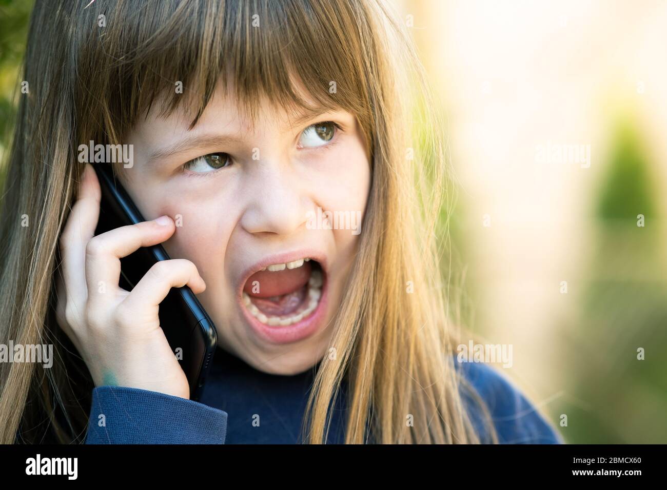 Portrait of angry child girl with long hair talking on cell phone ...