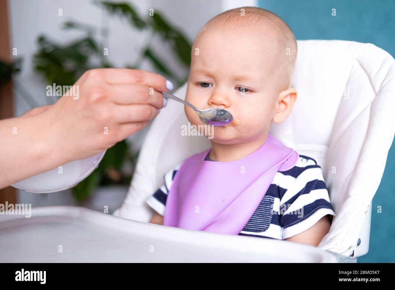 Sad baby eating tasteless food. Mom feeds little caucasian child on ...