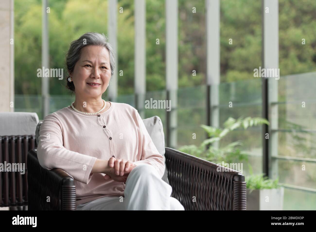 An Asian elderly woman sitting on a chair outdoors Stock Photo - Alamy