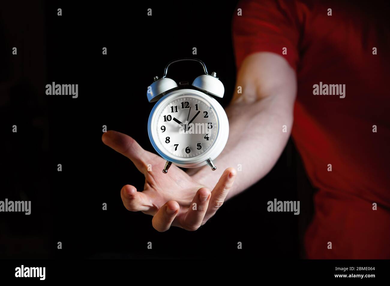 White retro alarm clock hovering above Caucasian male hand against dark ...