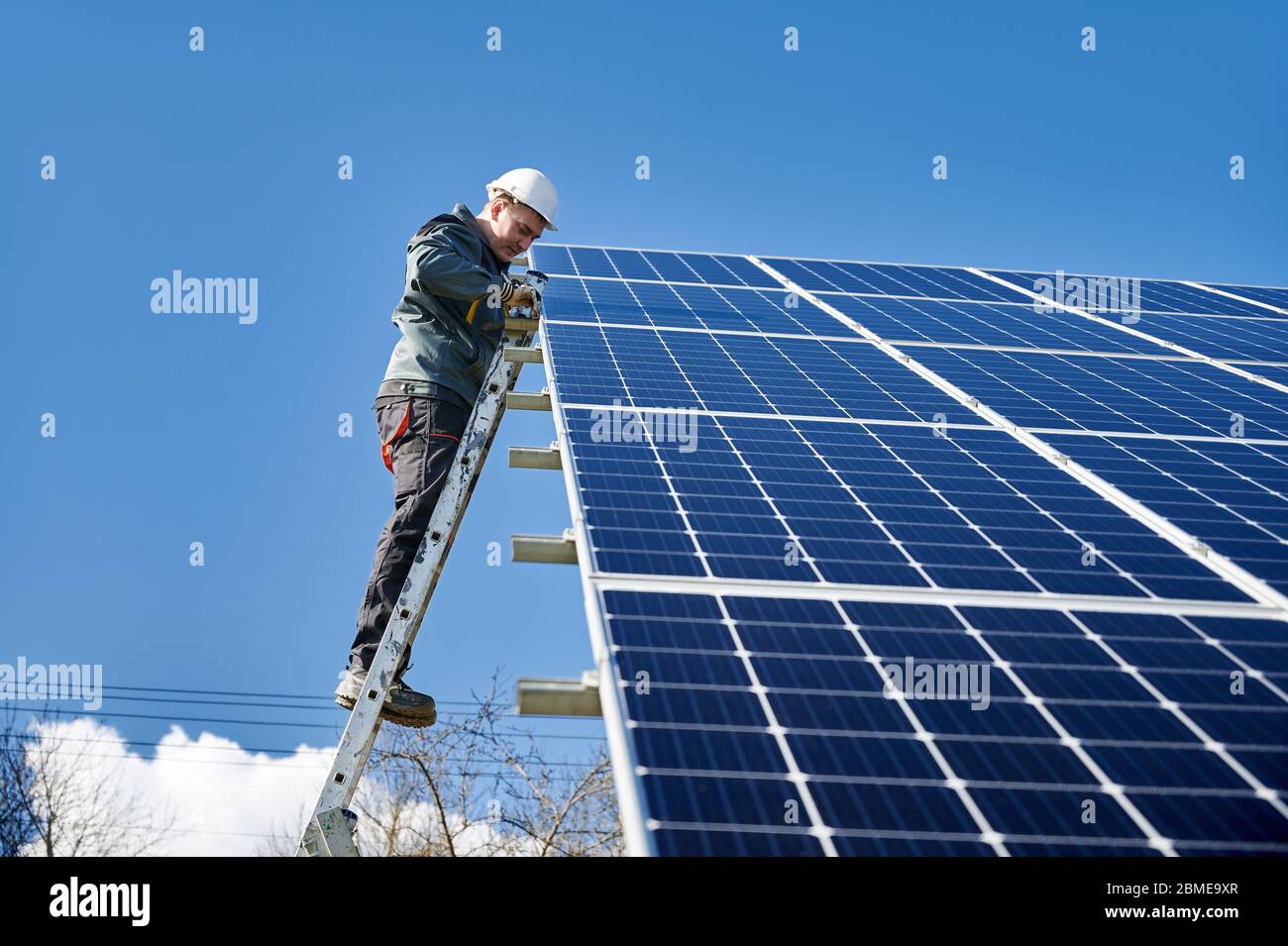 Electrician on ladder installing photovoltaic solar panel under blue ...