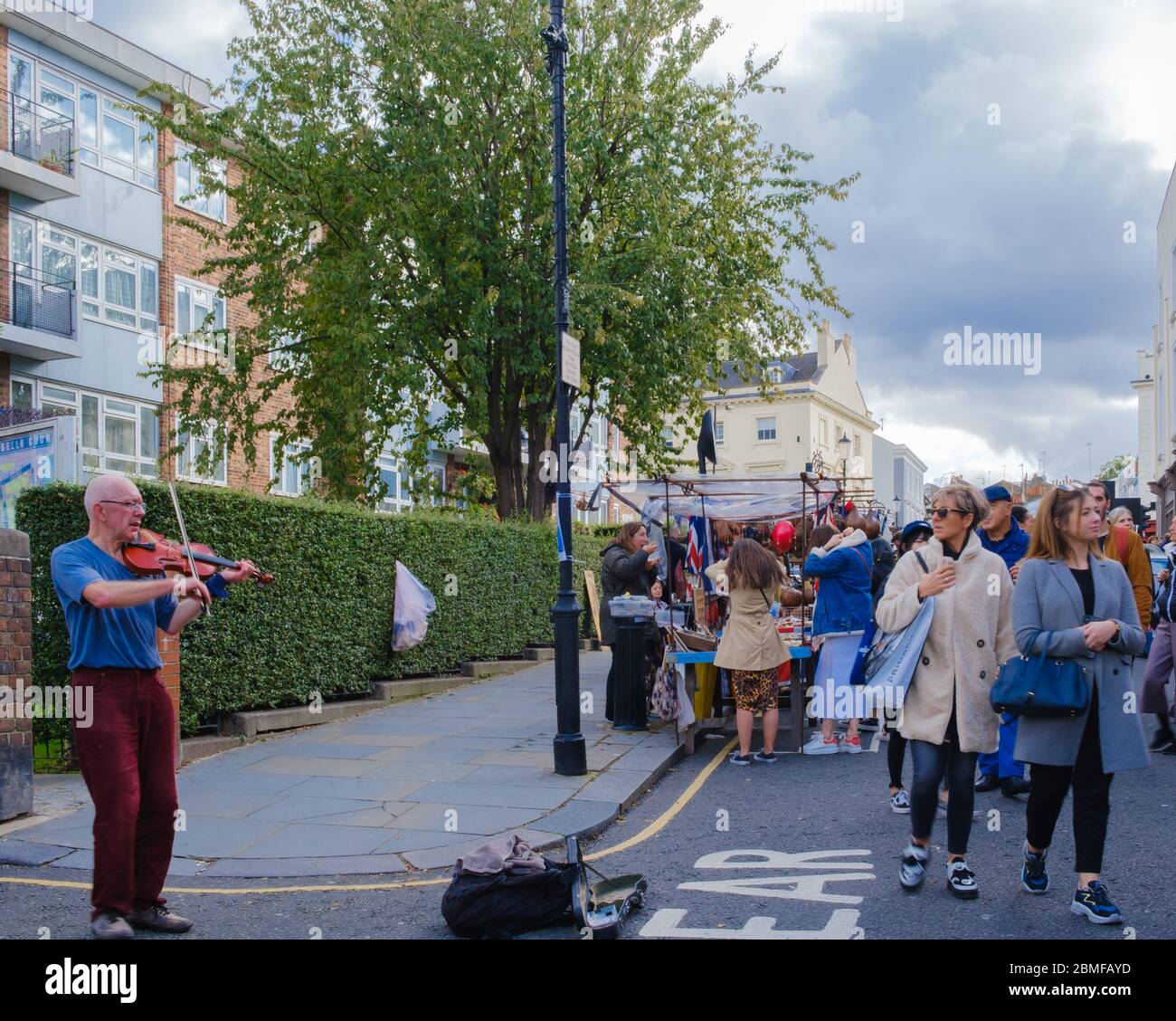 Street busker plays the violin while shoppers walk along Portobello ...