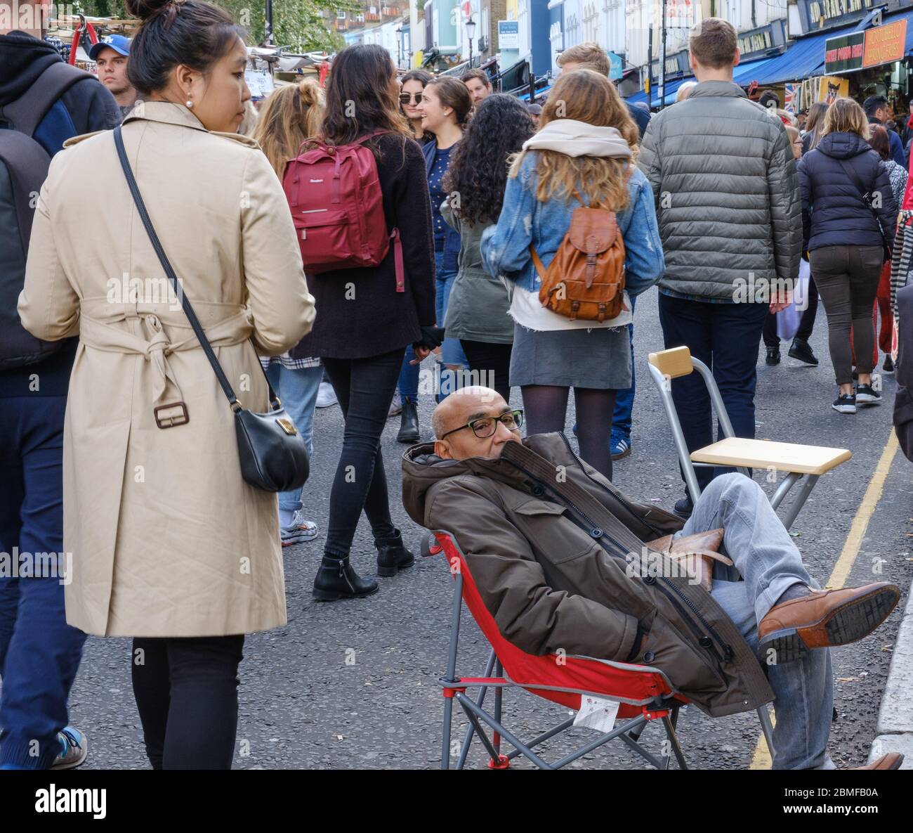 Crowds of shoppers at Portobello Market with sleepy man in chair ...