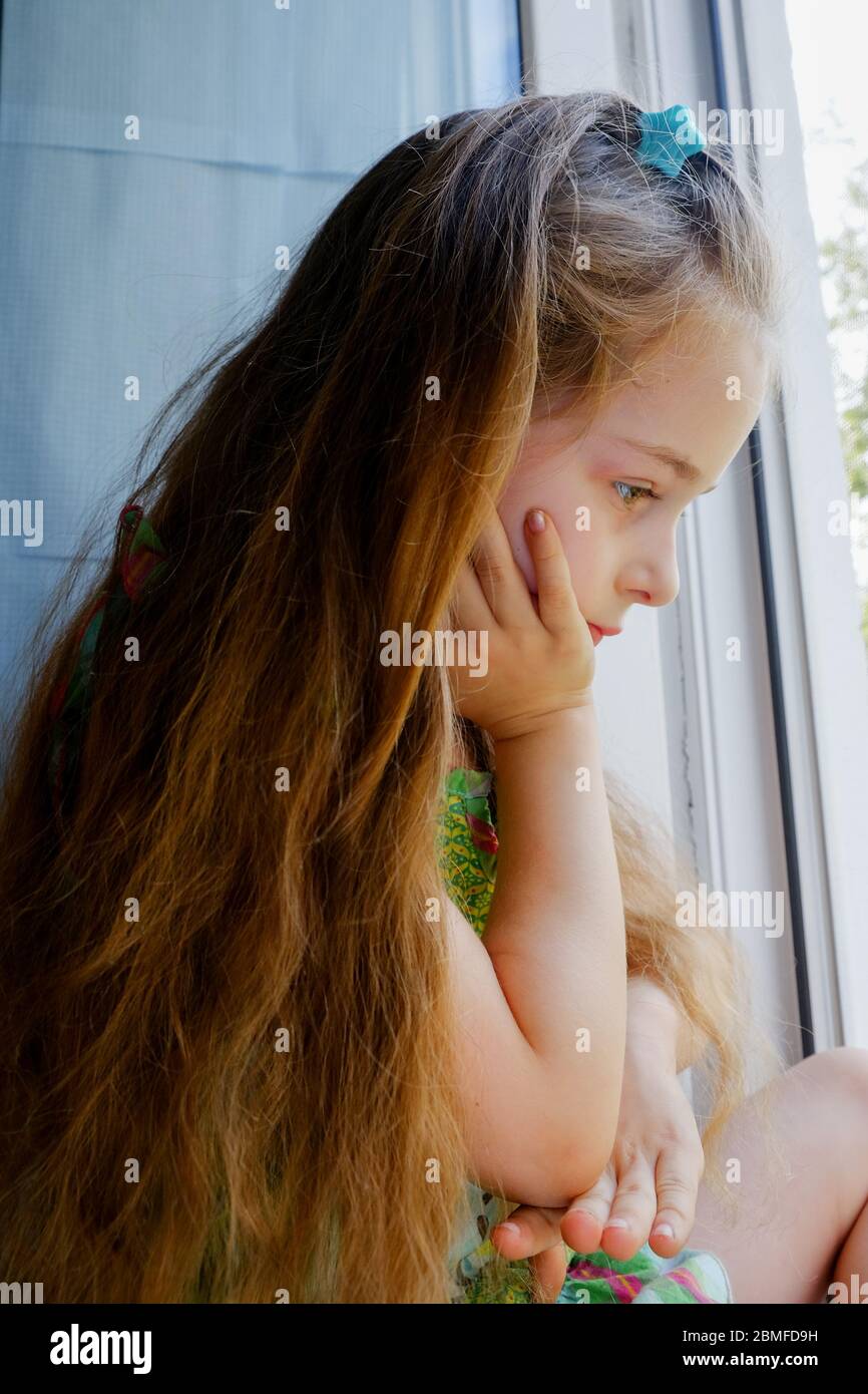 Little girl by the window. A 5 year old girl sits by the window at home ...