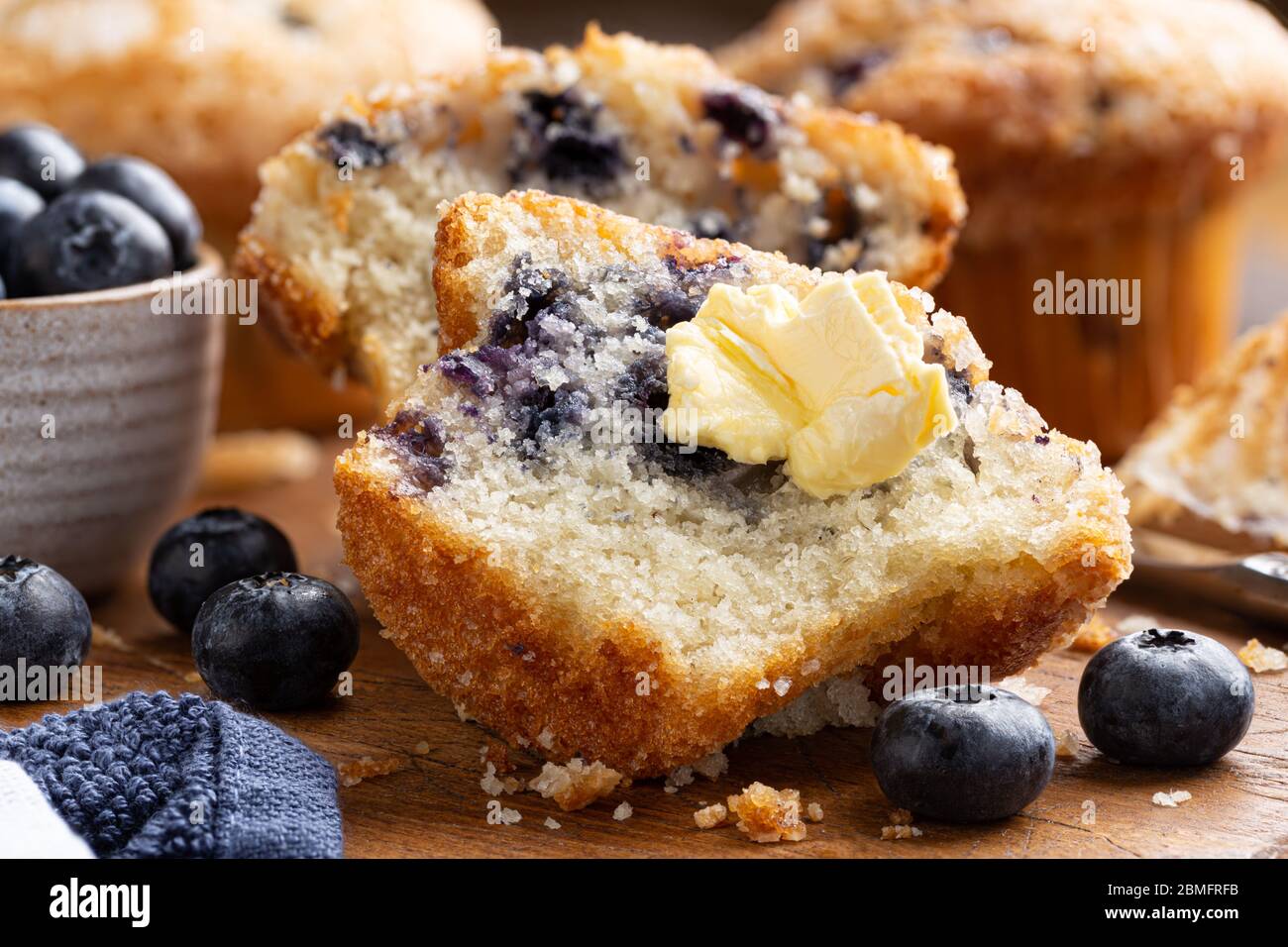 Closeup of a blueberry muffin cut in half with butter and fresh berries ...