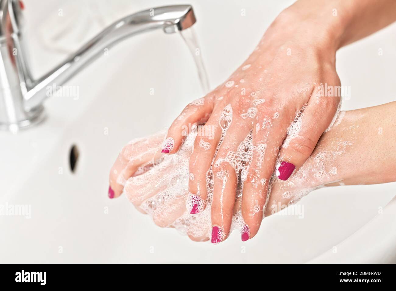 Young woman washing her hands under water tap faucet with soap. Detail ...