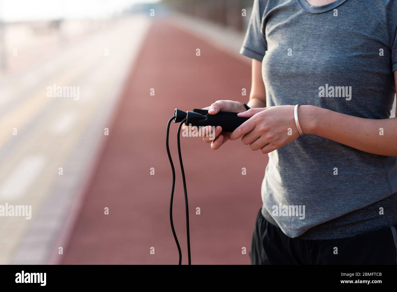 Woman holding a jumping rope on a running track before fitness training ...