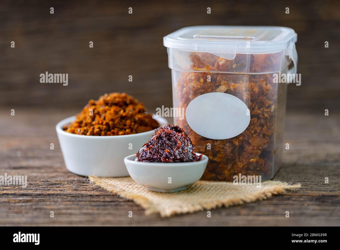 Spicy chili paste in white ceramic and plastic containers on wood ...
