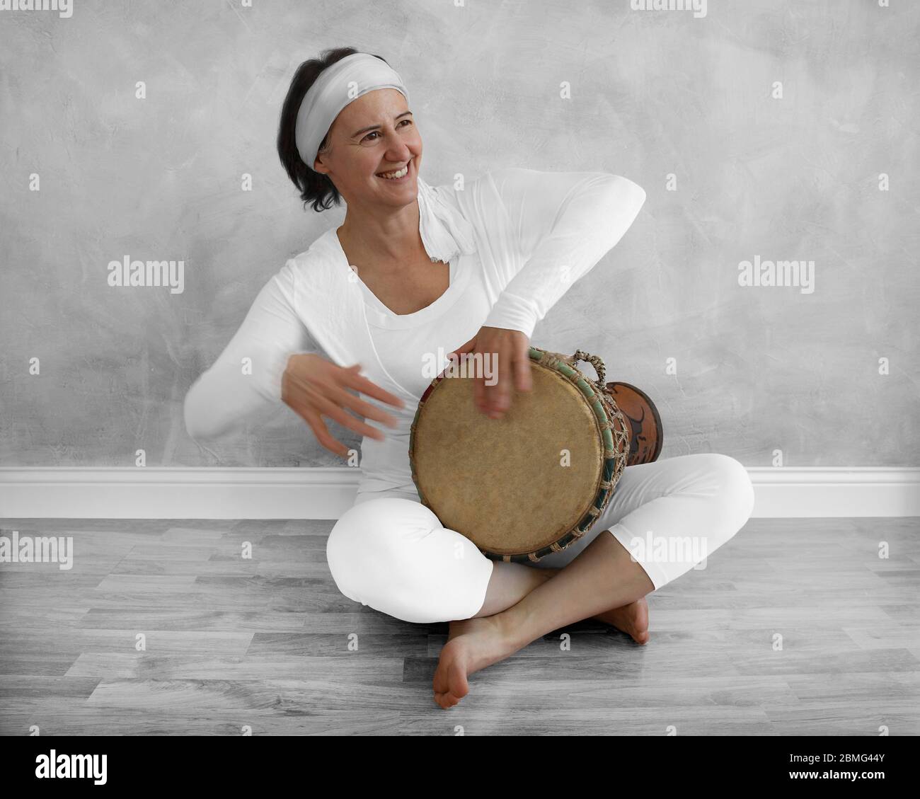 A smiling woman plays a sitting djembe drum Stock Photo - Alamy