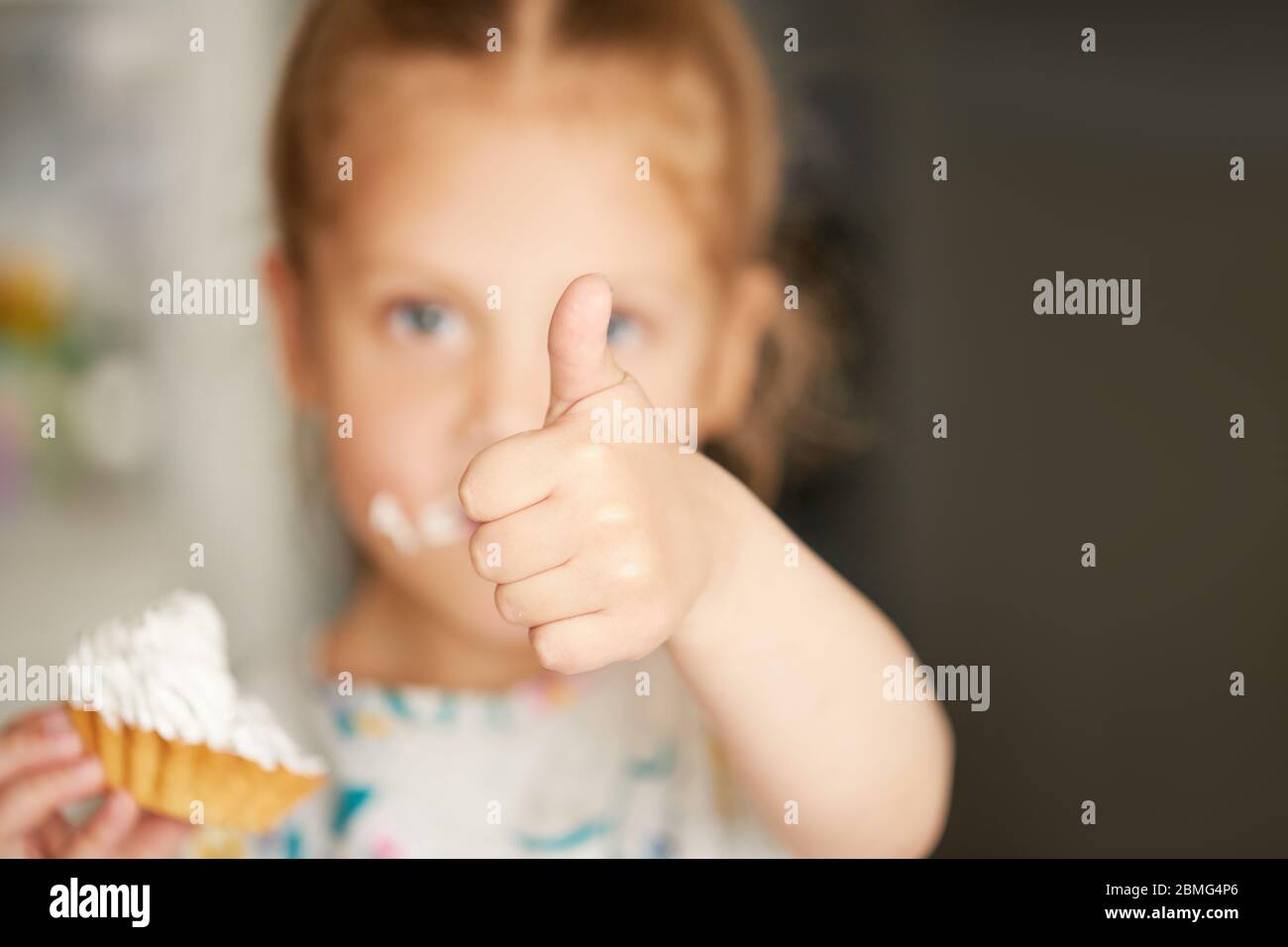 Cheerful smiling child girl eating a delicious cake and showing thumbs ...