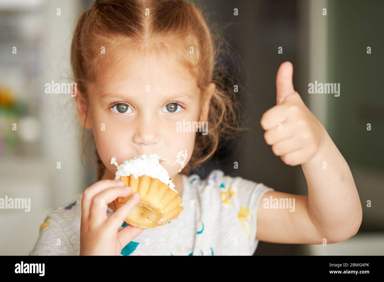 Cheerful smiling child girl eating a delicious cake and showing thumbs ...