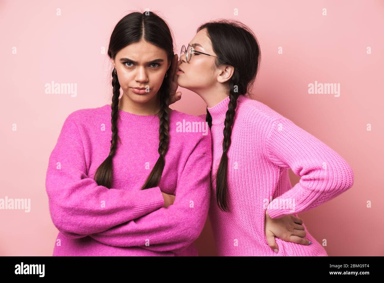 Two upset cute teenage girls standing isolated over pink background ...