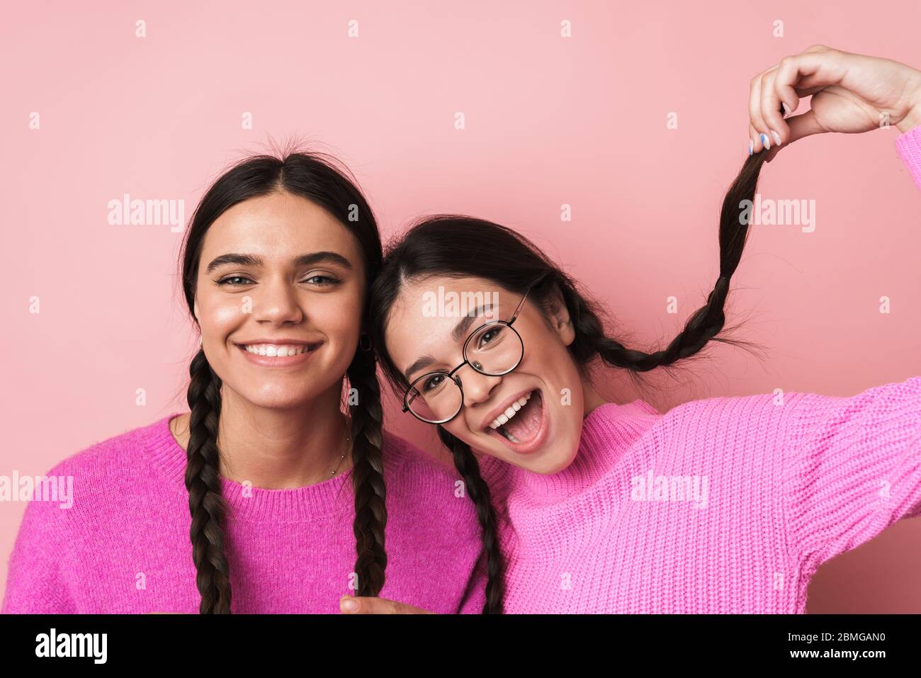 Two cheerful cute teenage girls having fun isolated over pink ...