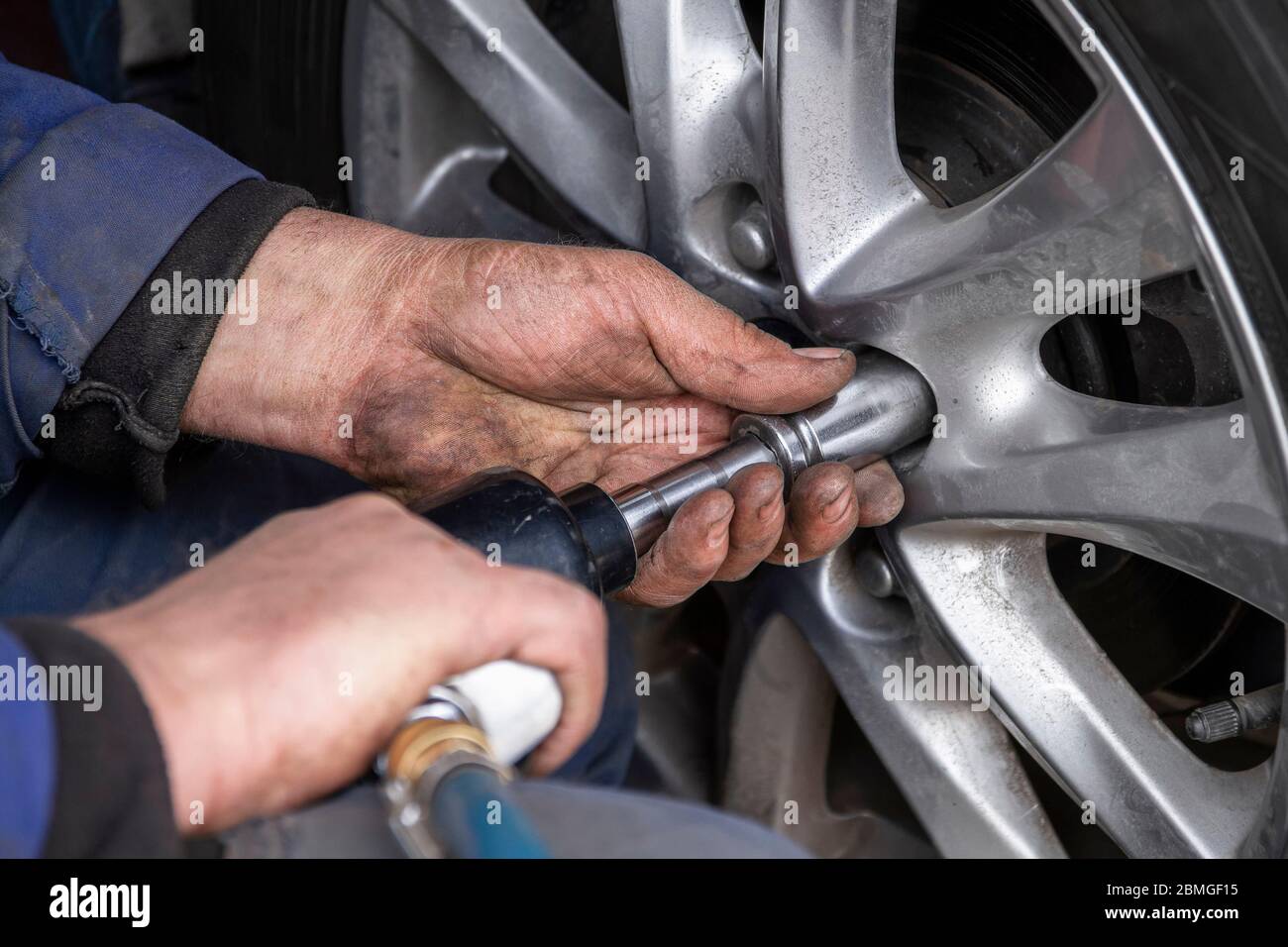 Mechanic without gloves is changing wheel on car with pneumatic wrench ...