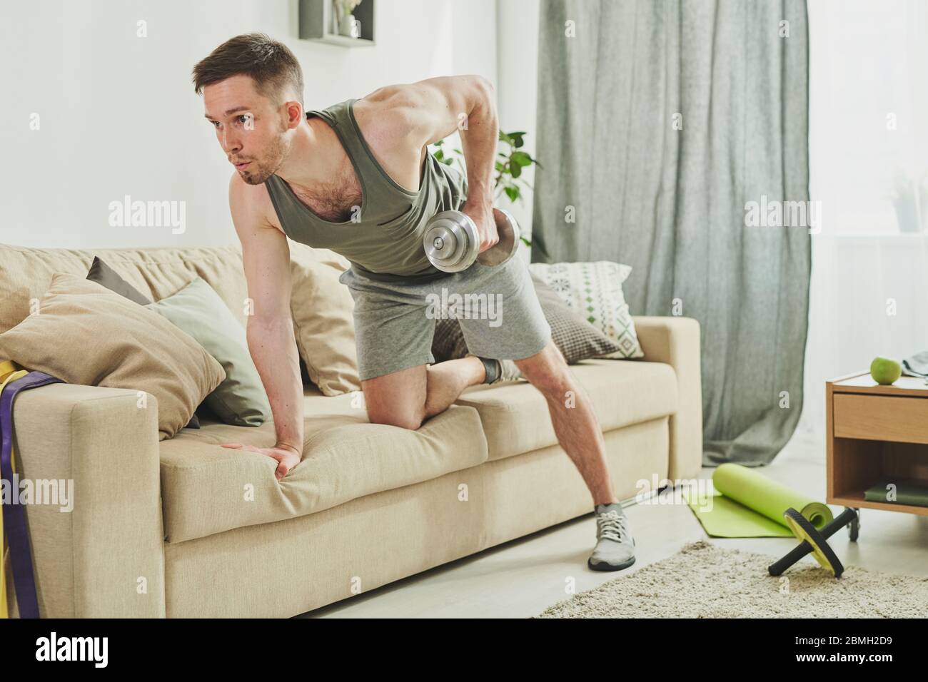 Young sportsman in activewear leaning on couch while doing exercise ...