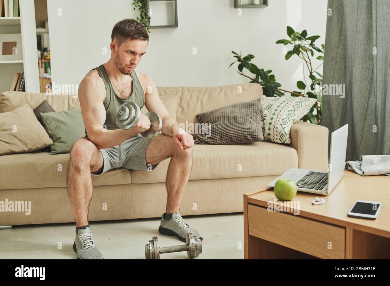 Young man in sportswear sitting on couch in front of laptop while doing ...