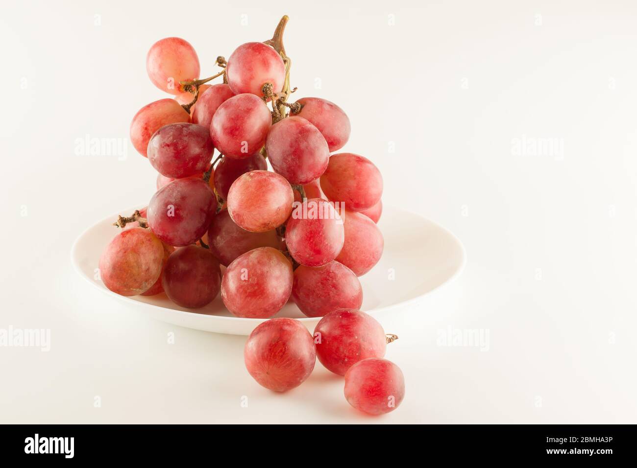 bunch of fresh grapes lies on a dinner plate on a white background ...