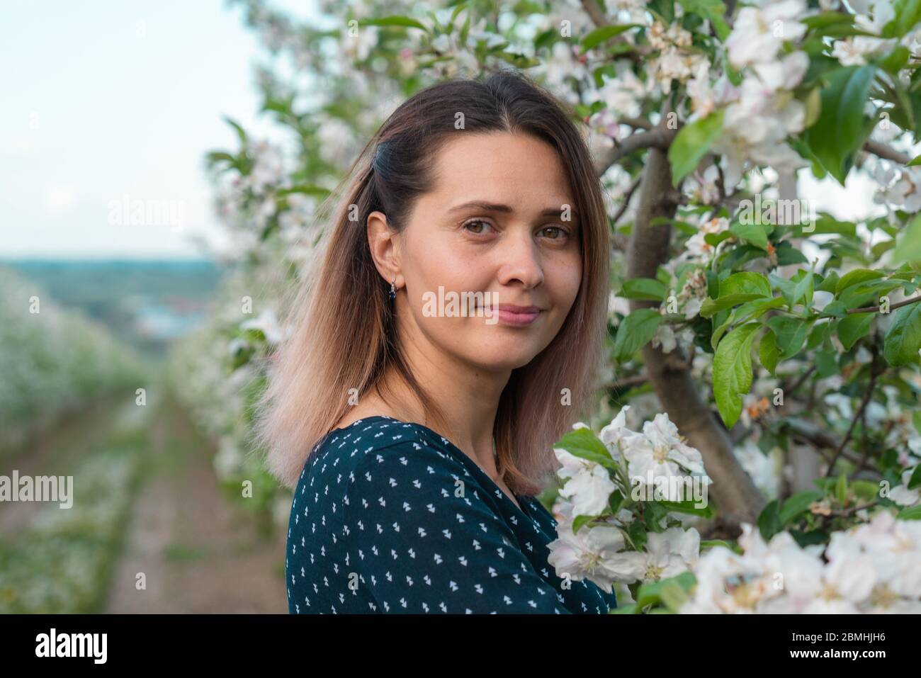 A beautiful and charming girl stands near a blossoming tree. Beautiful ...