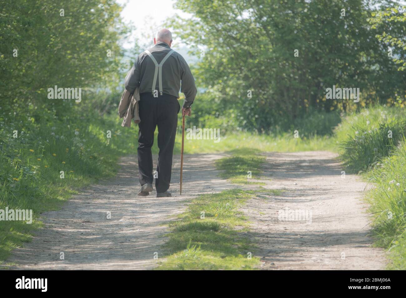 an old man walks along a country lane on a walking stick Stock Photo ...