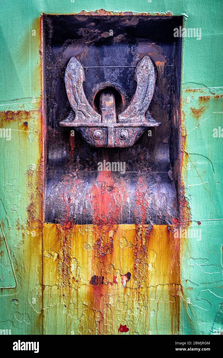 Rusty purple color anchor hanging on a rusted green and orange boat ...