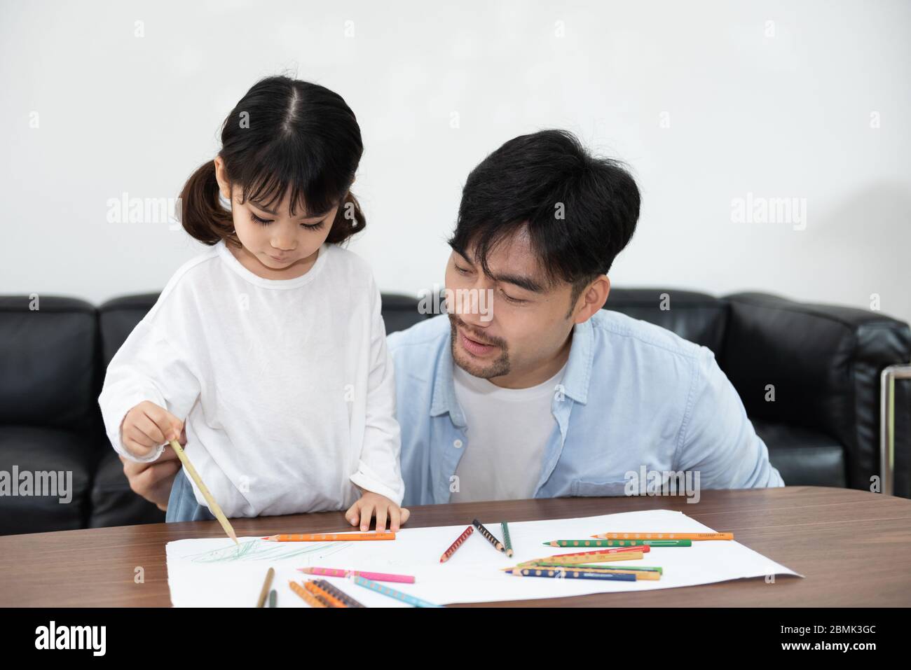 A pair of young Asian father and daughter are drawing in the living ...