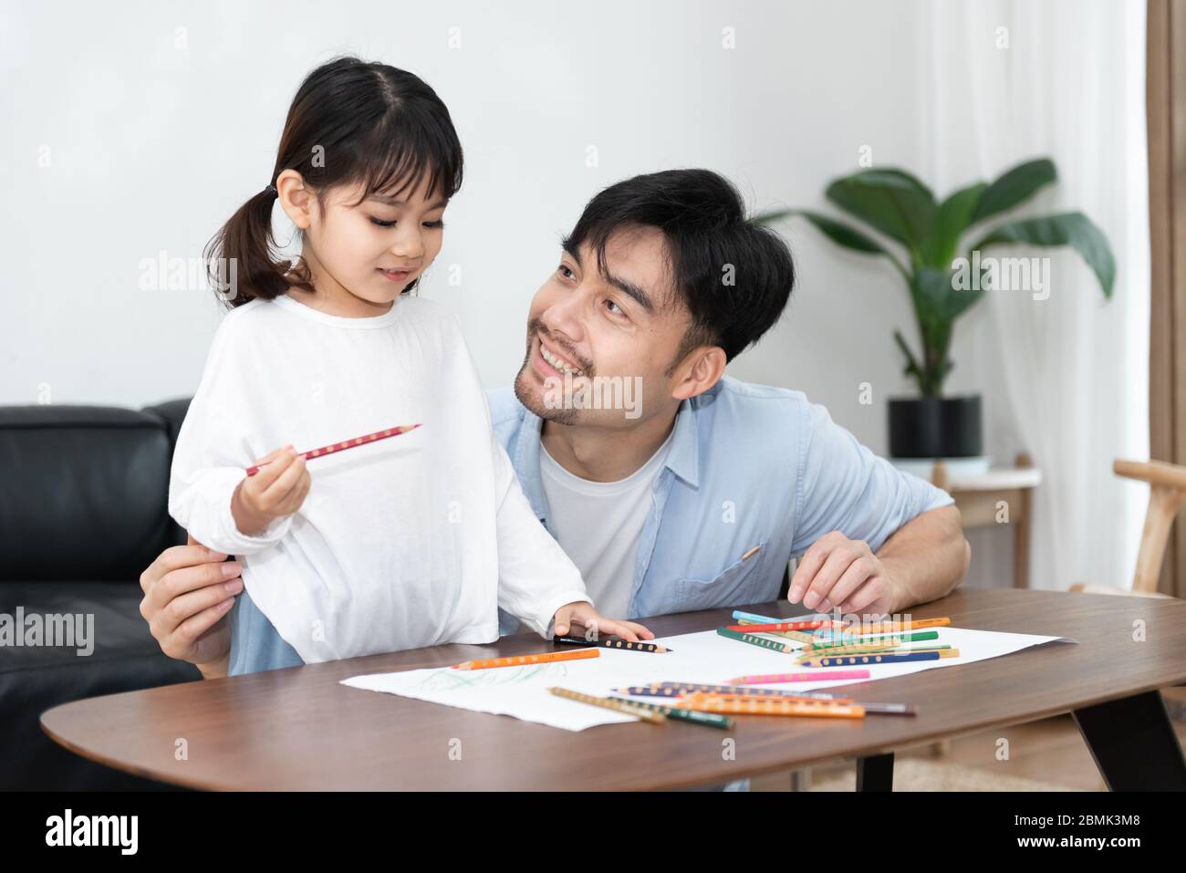 A pair of young Asian father and daughter are drawing in the living ...