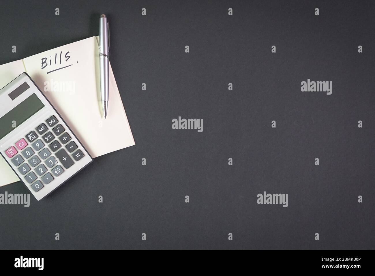Calculator on top of notepad with the words Bills. Black background ...