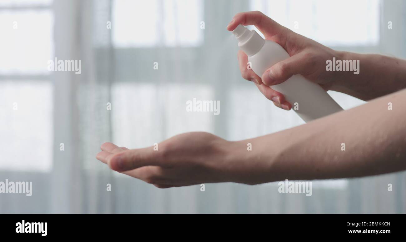 man spraying sanitizer on his hands standing in front of the window ...