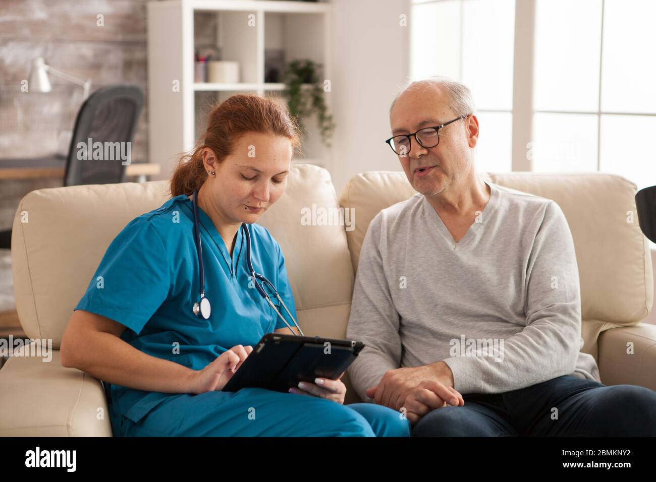 Female nurse in nursing home helping old man to use tablet computer ...