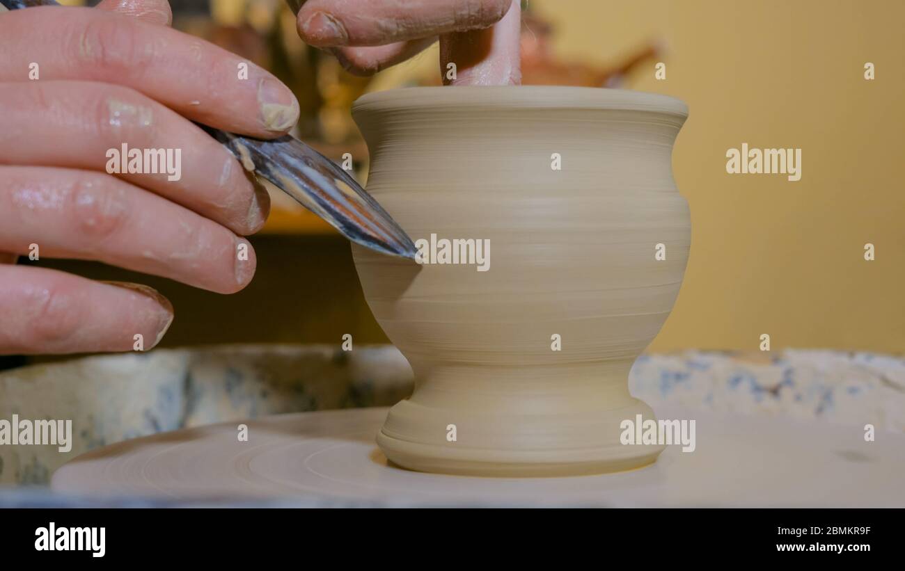 Professional male potter shaping mug with special tool in pottery ...